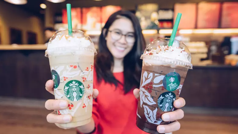 Femeie ținând în mână două Frappuccinos de vacanță Starbucks