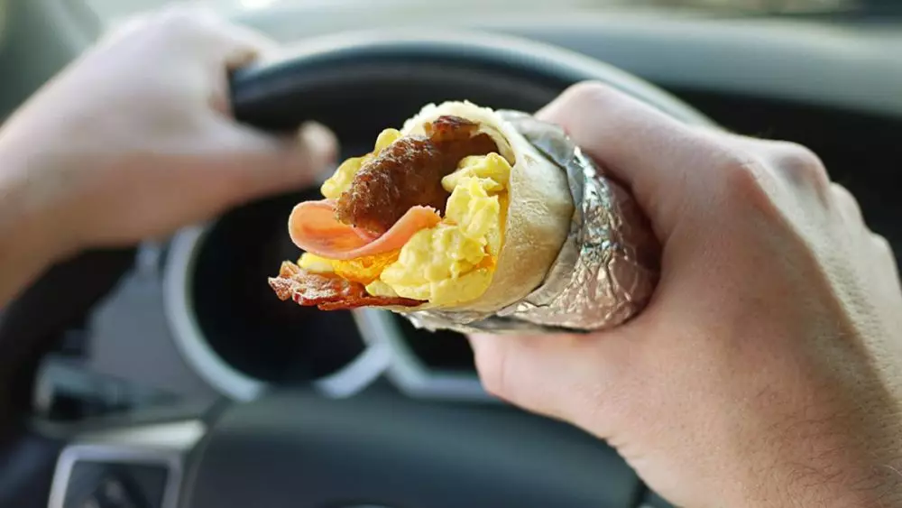 Jack in the Box kifungua kinywa burrito mkononi mwa mwanamume anayeendesha gari