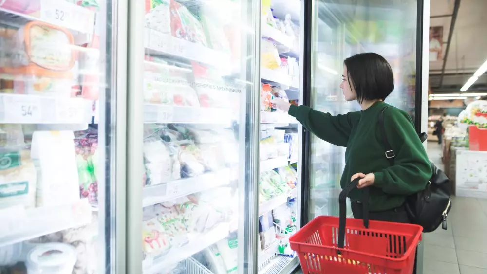 Una donna cerca i cursori nel corridoio del congelatore del negozio di alimentari.