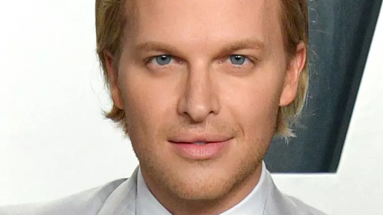 Ronan Farrow ridetanta en arĝenta smokingo