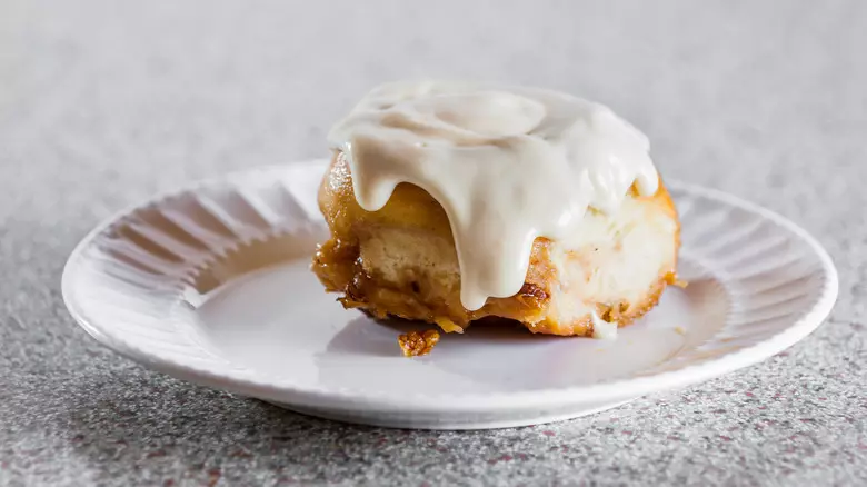 Cinnamon roll trochdrenkt yn glazuur op in wite plaat