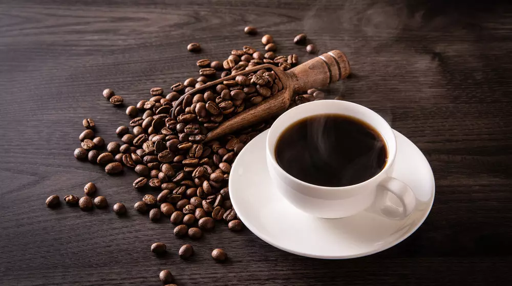 Melnas kafijas tase, ko ieskauj kafijas pupiņas