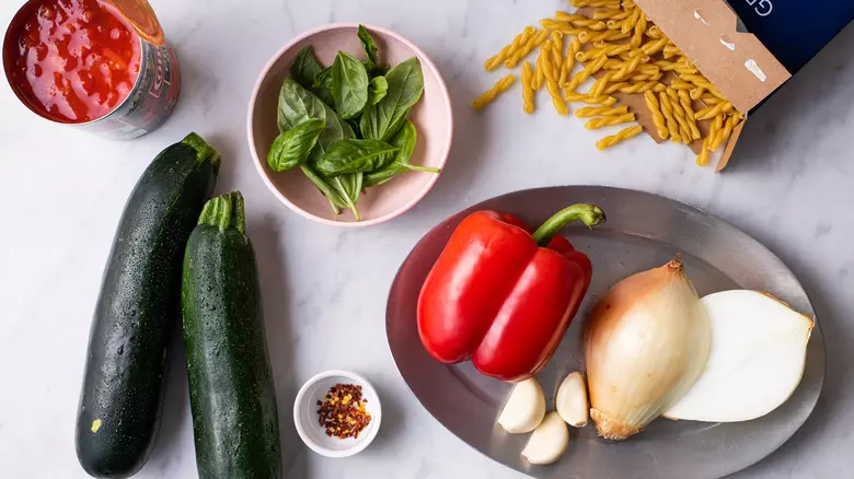 Ingrédients réunis sur un comptoir en marbre pour faire des pâtes aux légumes d'été.