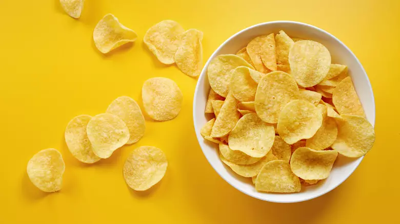 Kartoffelchips in weißer Schüssel vor gelbem Hintergrund