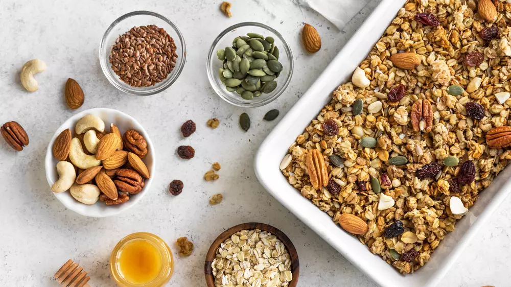 Granola en un plat de forn blanc al costat de bols de fruits secs