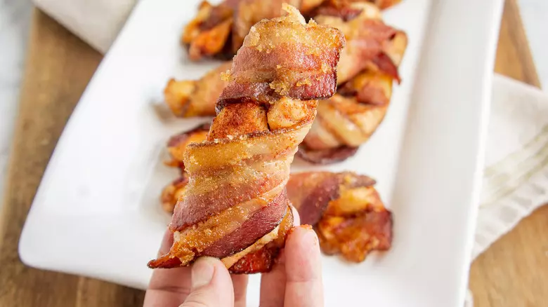 piletina umotana u slaninu koja se drži u ruci iznad tanjura
