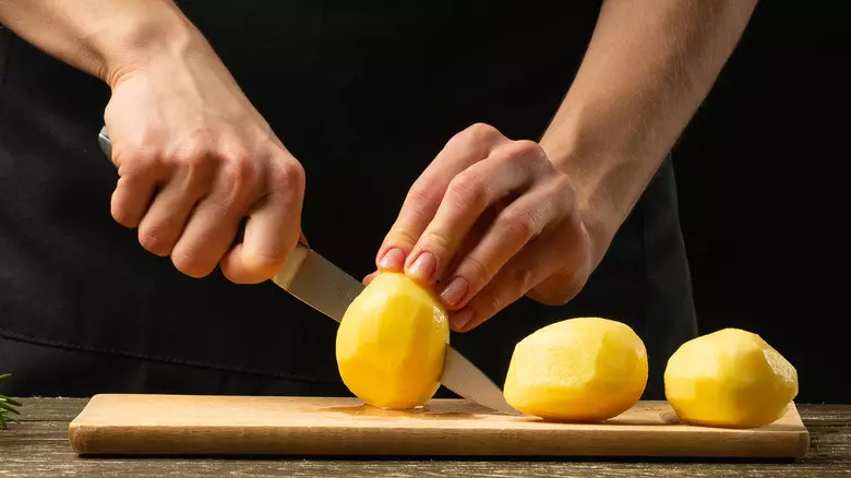 Ruky krájajú ošúpané zemiaky nožom