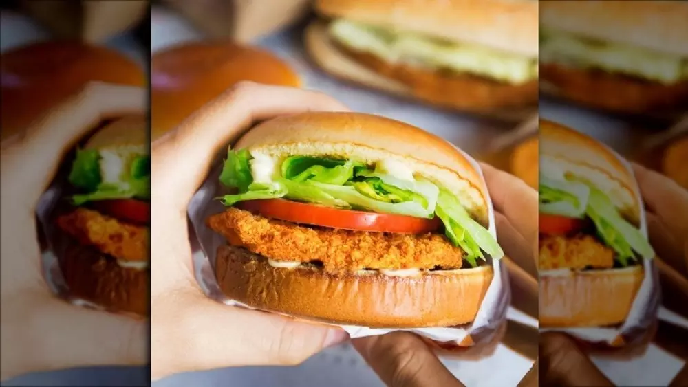 Hand, die das alte knusprige Hähnchen-Sandwich hält