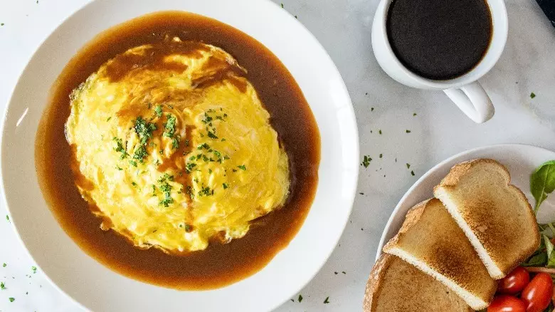 Omurice σε σάλτσα demiglace στο πιάτο με καφέ, τοστ και σαλάτα