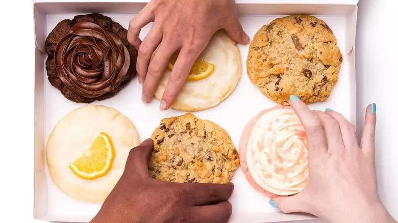 Mãos alcançando biscoitos Crumbl