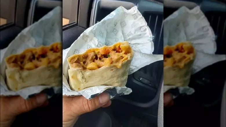 Iemand wat 'n Del Taco Epic Loaded Queso Burrito in die motor vashou