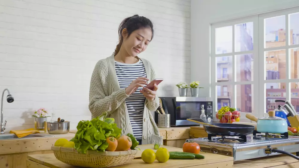 wanita memasak dengan telefon pintar sayur-sayuran