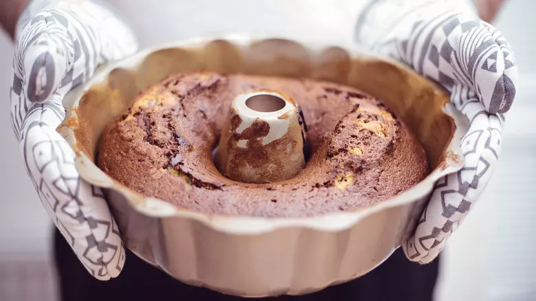 Mains dans des gants de cuisine tenant un moule à gâteau bundt