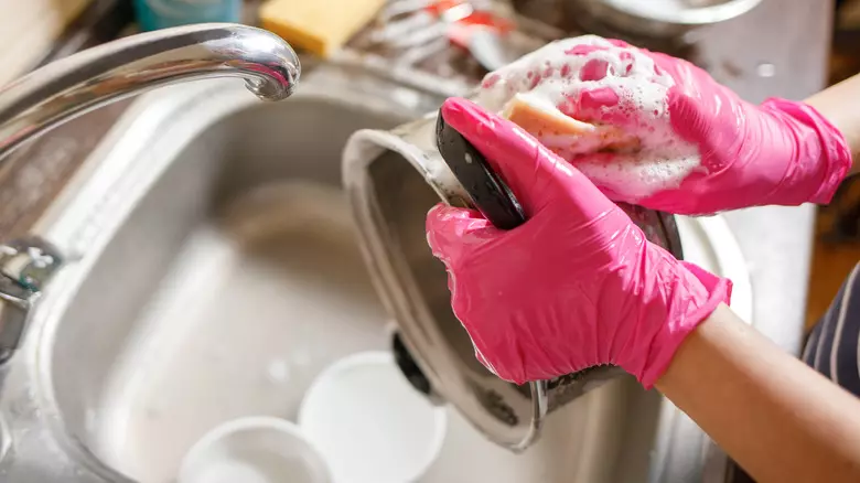 गुलाबी हातमोजे घालून भांडे साफ करणारी व्यक्ती
