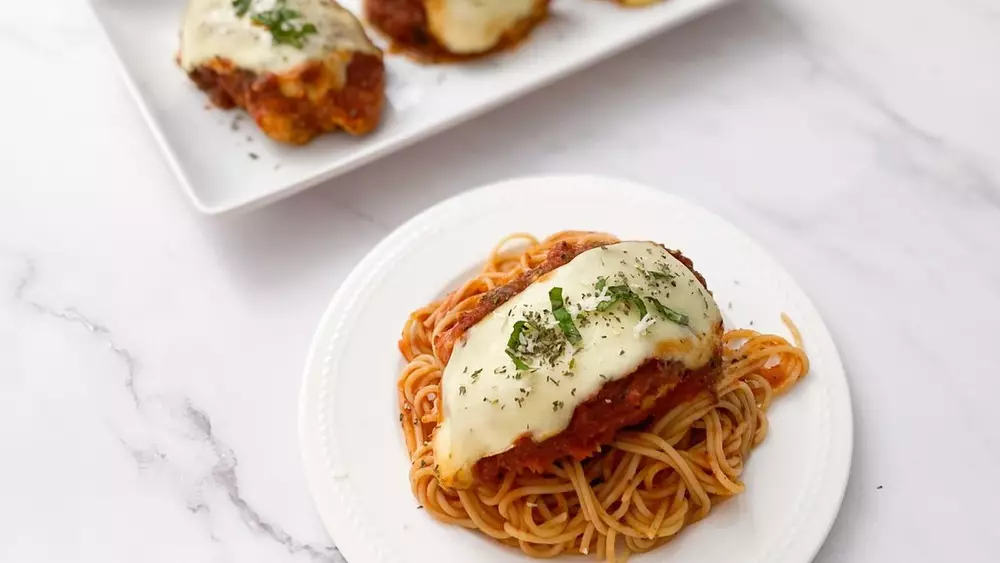 chicken Parmesan op in bêd fan spaghetti noedels