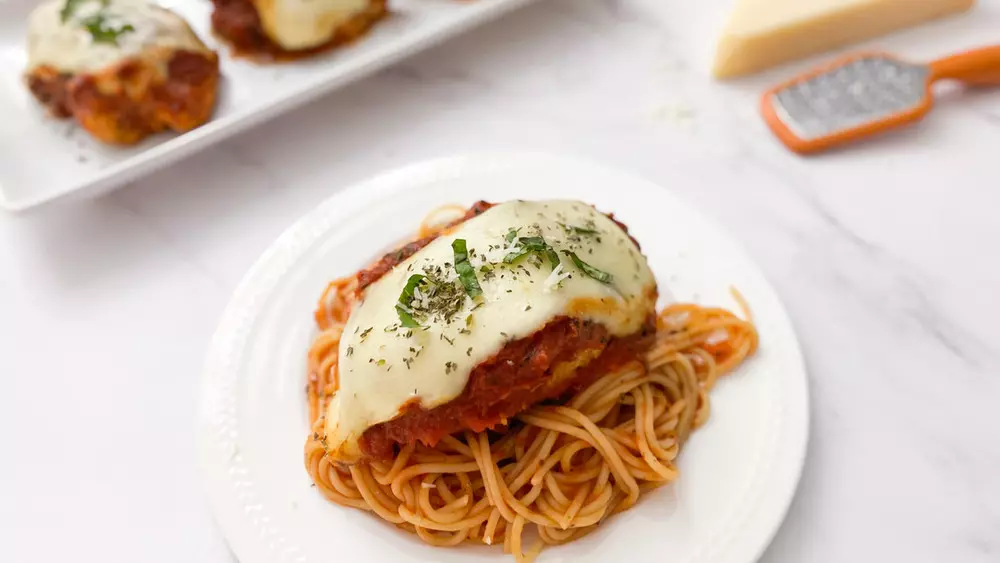 kip Parmesan sittend op in bêd fan saus en spaghetti noedels op in wite plaat sittend op in wyt en griis oanrjocht