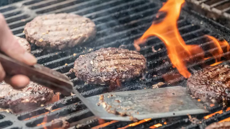 Person som vänder hamburgare på en grill