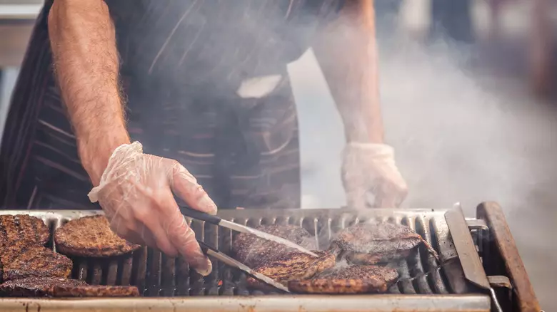 Mtu anayepika burgers kwenye grill nyeusi