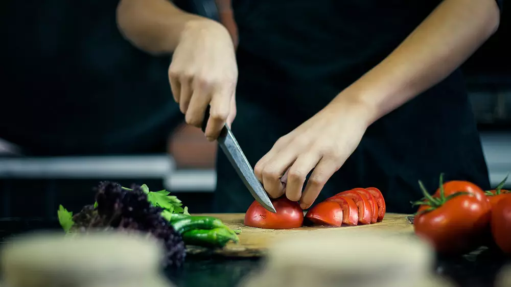 Mani che tagliano il pomodoro con la presa dell'orso