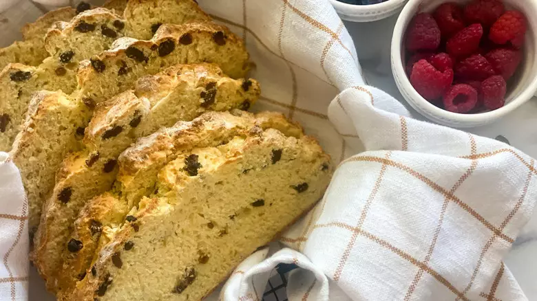 llesques de pa de refresc irlandès tradicional en una cistella folrada de tovalloles prop d'un bol blanc de gerds vermells madurs