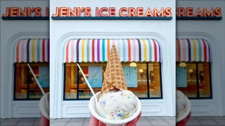 En hånd, der holder en kop is med en kegle i foran en Jeni's Splendid Ice Creams placering