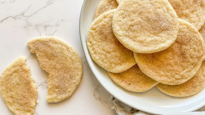 Une assiette pleine de biscuits snickerdoodle et un biscuit cassé sur la table.