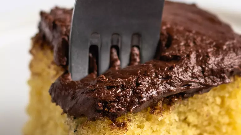 Gaffel i firkant af gul kage med tyk chokoladefrosting