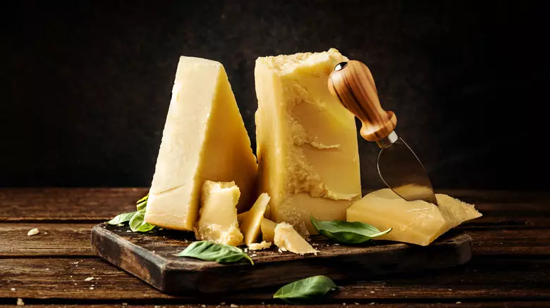 Bloques de queso parmesano en una tabla de madera con hojas de albahaca