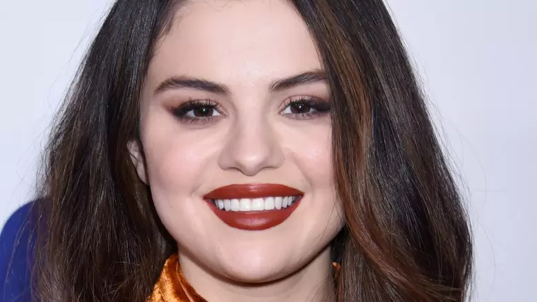 Selena Gomez klæddist rauðum varalit og brosir þegar hún situr fyrir á viðburði.