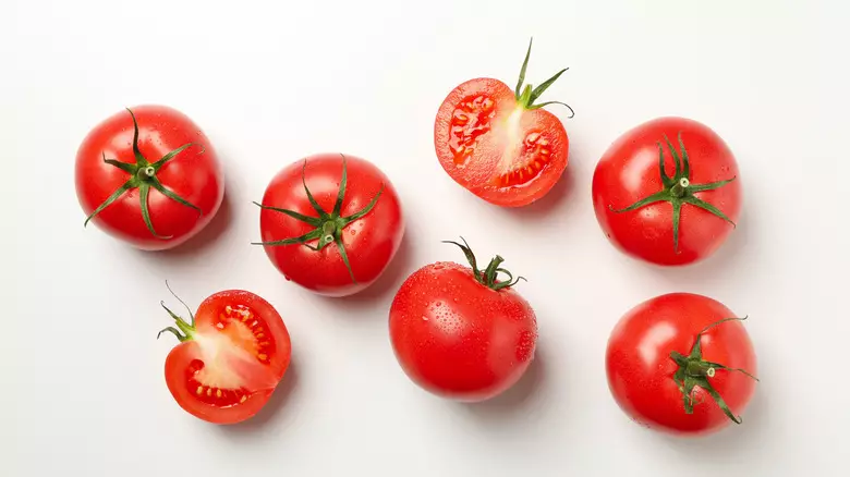 Tomates enteros y cortados a la mitad sobre fondo blanco.