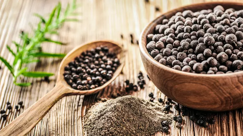 Grains de poivre noir dans un bol et une cuillère en bois