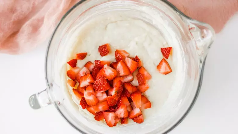 Fotografía cenital de masa para panqueques con fresas picadas encima en una taza medidora de vidrio