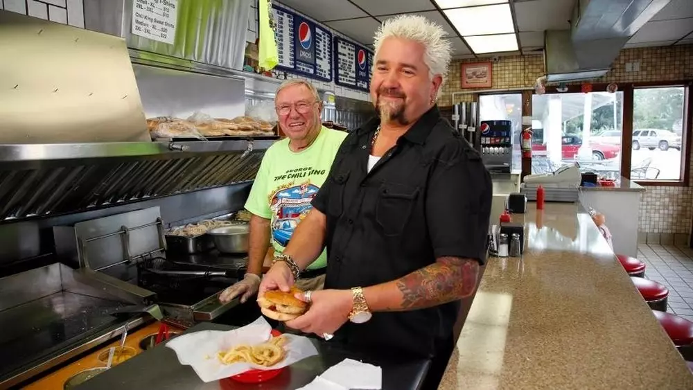 Guy Fieri lächelt und hält ein Sandwich
