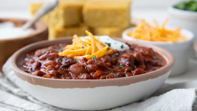 bönchili i en skål toppad med riven ost och gräddfil och serverad med majsbröd