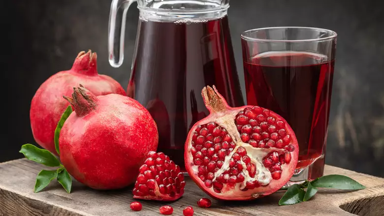 nar, biri ikiye bölünmüş, sürahi ve bir su bardağı nar suyu