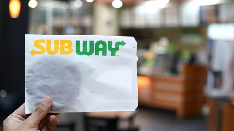 Cwci isffordd mewn papur lapio yn cael ei ddal i fyny mewn bwyty Subway