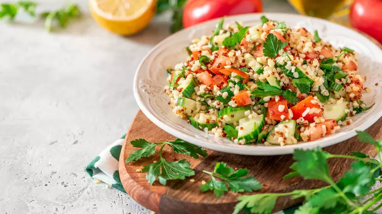 insalata di cous cous in una ciotola bianca con pomodori, cetrioli e prezzemolo