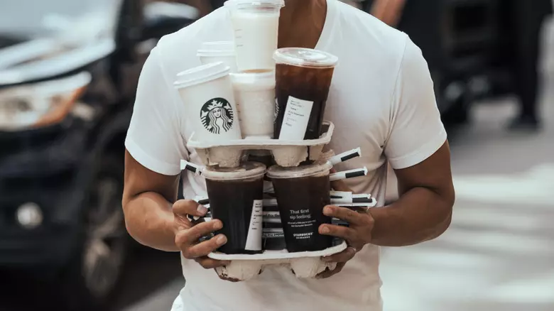 мужчина балансирует слишком много чашек Starbucks