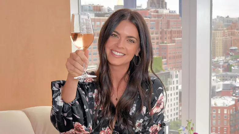 Katie Lee zvedá sklenku vína s panorámou města v pozadí