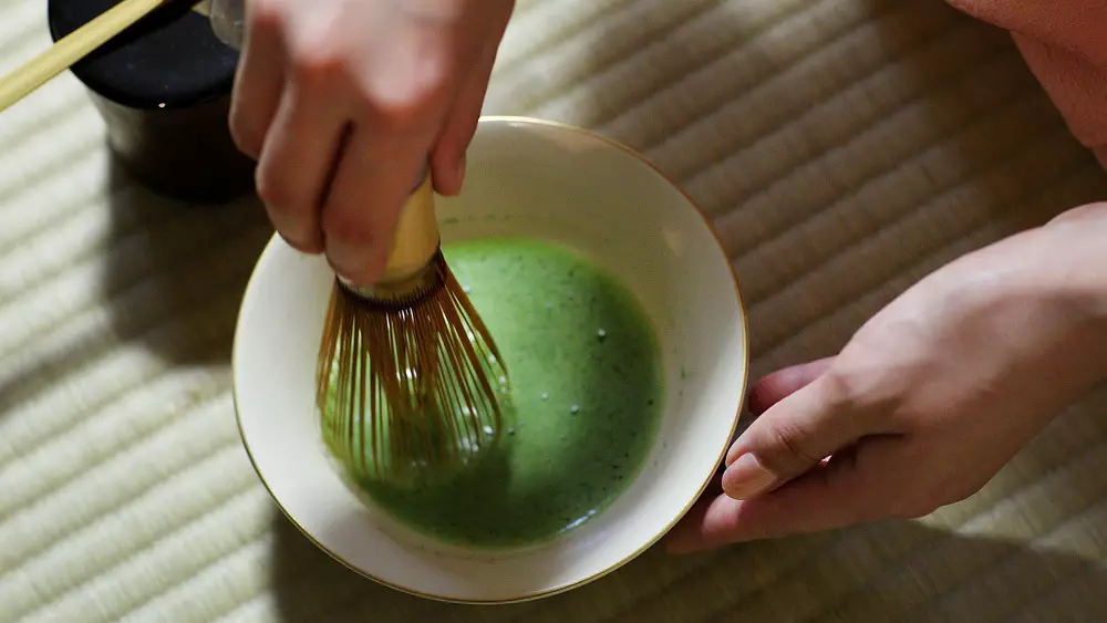 Hände bereiten Matcha mit Schneebesen vor