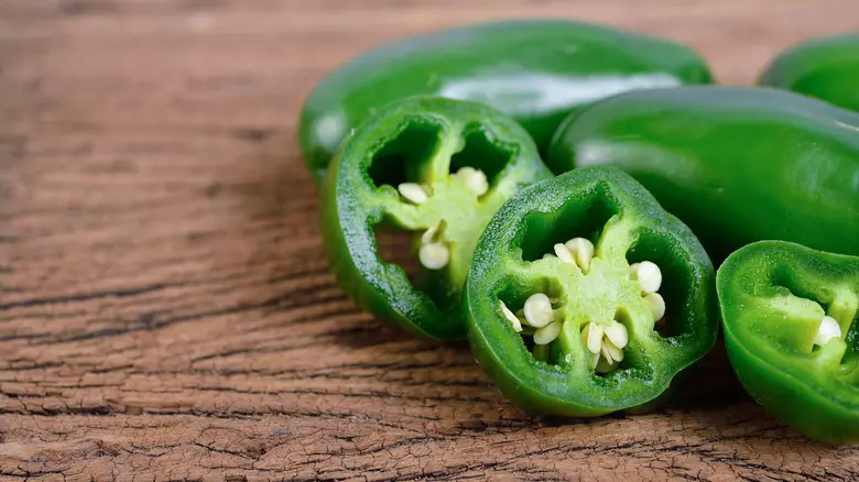 Kokonaisia ja viipaloituja jalapeñoja puupinnalla