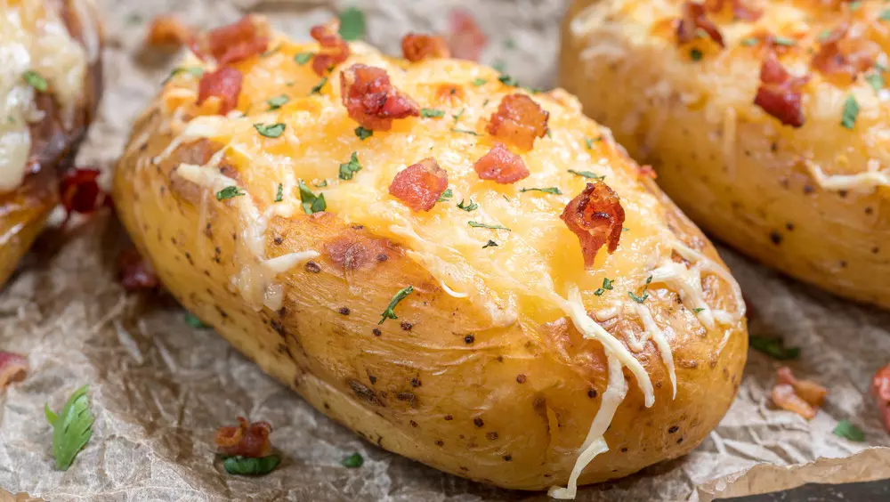 Beladene gebackene Kartoffeln, bedeckt mit Käse, Schnittlauch und Speck