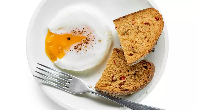 Posjert egg og toast på hvit tallerken med gaffel