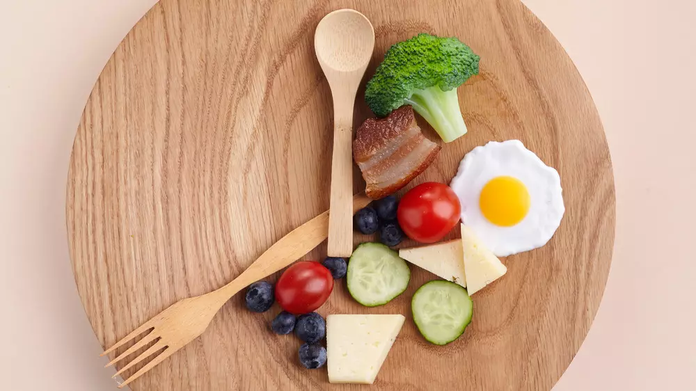Placa de madeira e utensílios cercados por legumes, ovo e bacon