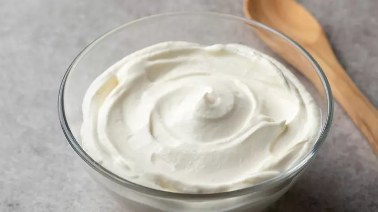 Crème fraîche naturel in een kom met een houten lepel erachter