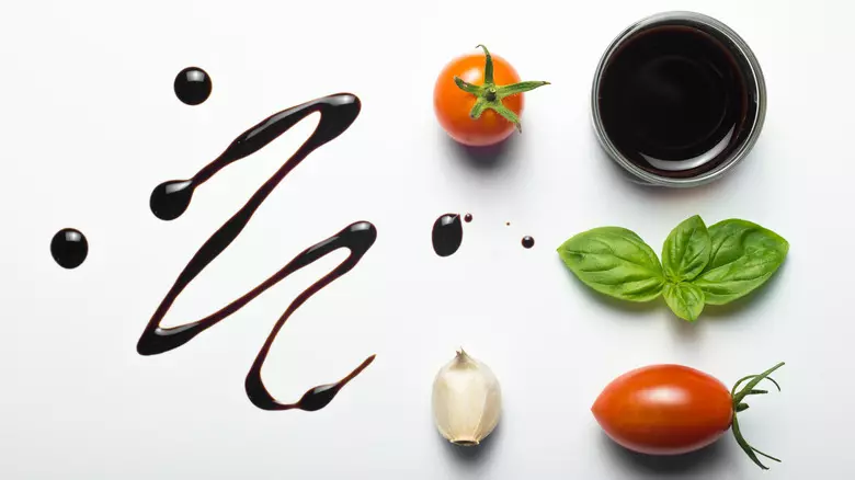 Rocíe vinagre balsámico junto al arreglo de tomates, diente de ajo, hojas de albahaca y tazón de vinagre balsámico