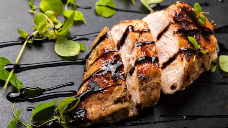 Pollo cocido con llovizna balsámica y microvegetales sobre un fondo gris oscuro