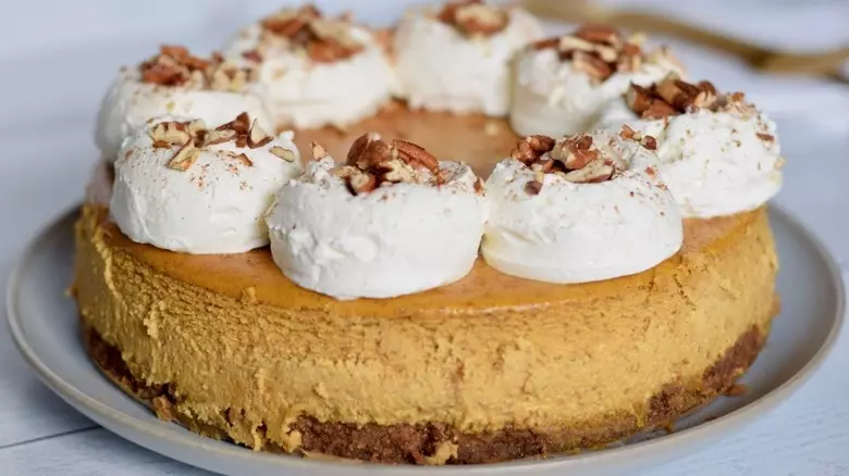 Pumpkin Cheesecake na nilagyan ng mga dollops ng whipped cream at mga piraso ng pecan