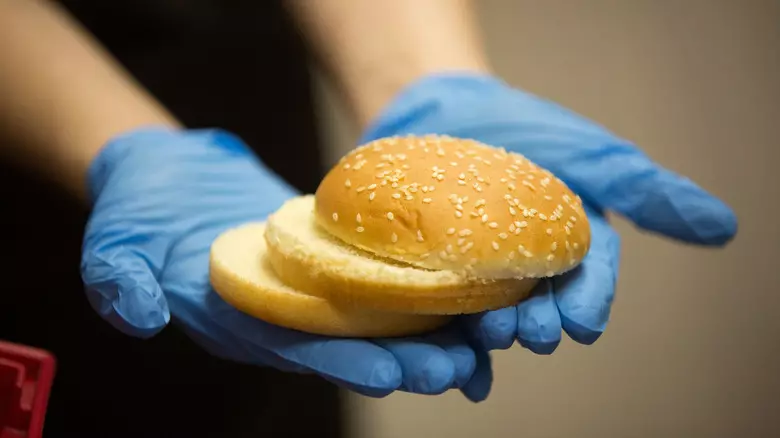 Awọn ọwọ pẹlu awọn ibọwọ buluu ti o ni hamburger bun