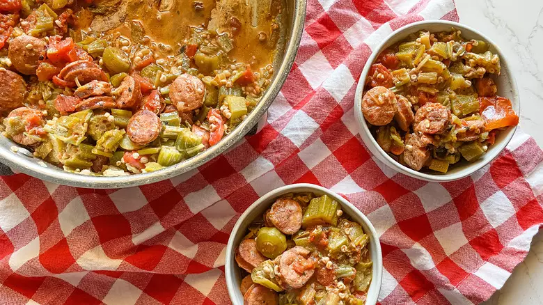 Toma aérea dunha cunca metálica e dúas cuncas máis pequenas cheas de okra guisada e tomates con salchicha